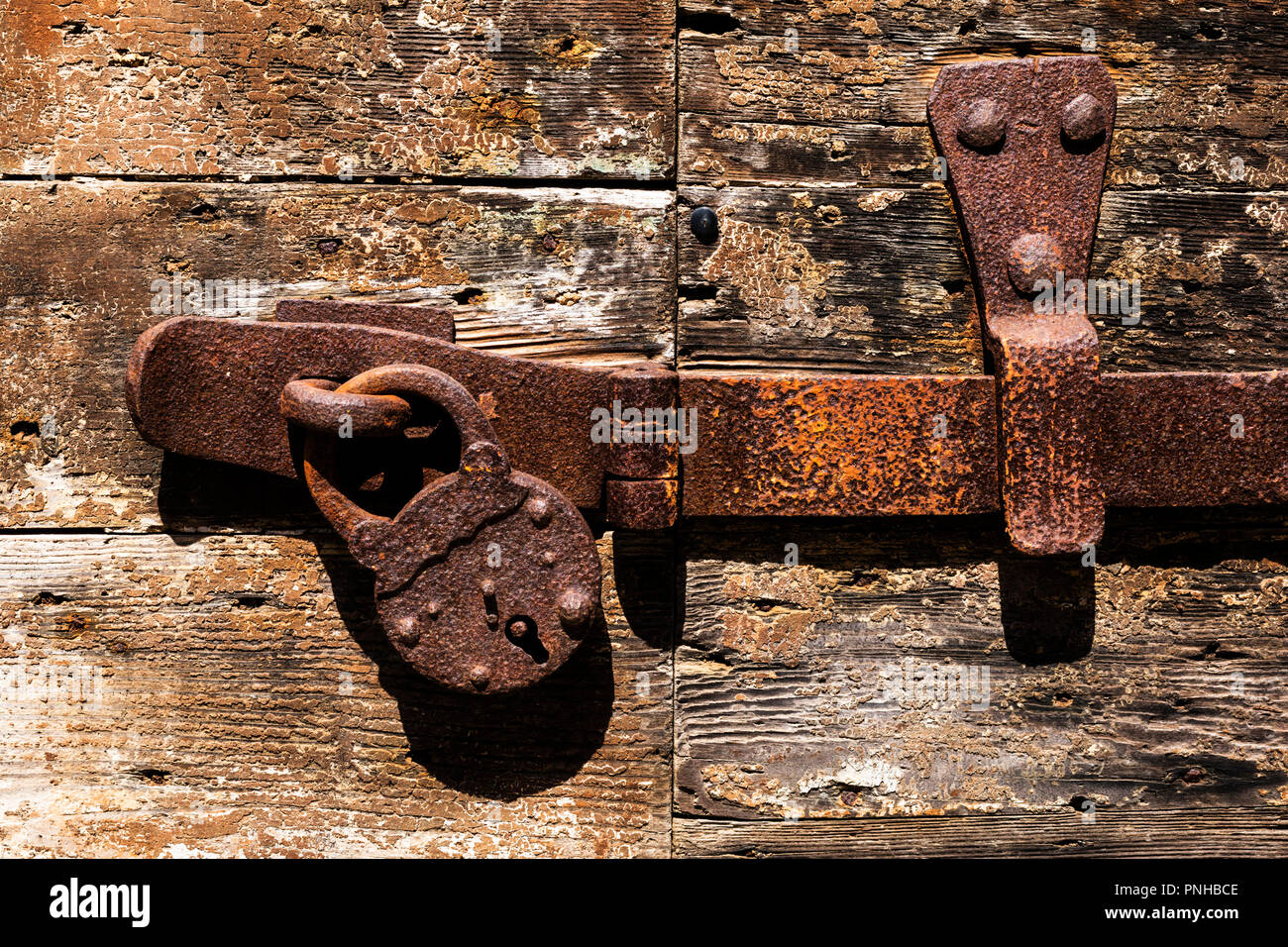 Ancient rusty bolted weathered wooden door padlocked shut in baking ...