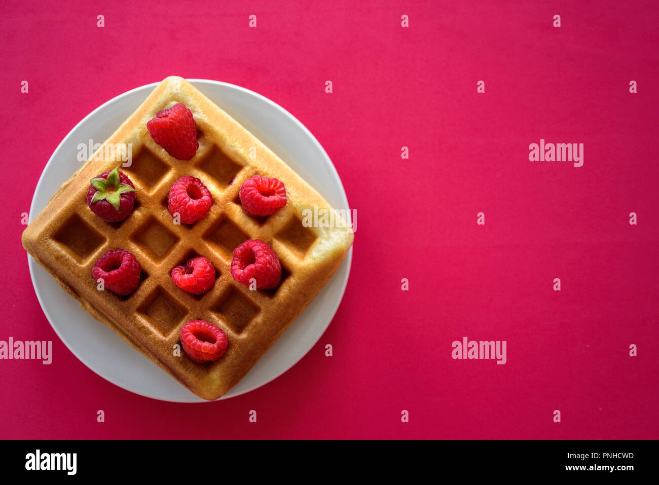 Belgian waffles with raspberries on red background Stock Photo - Alamy