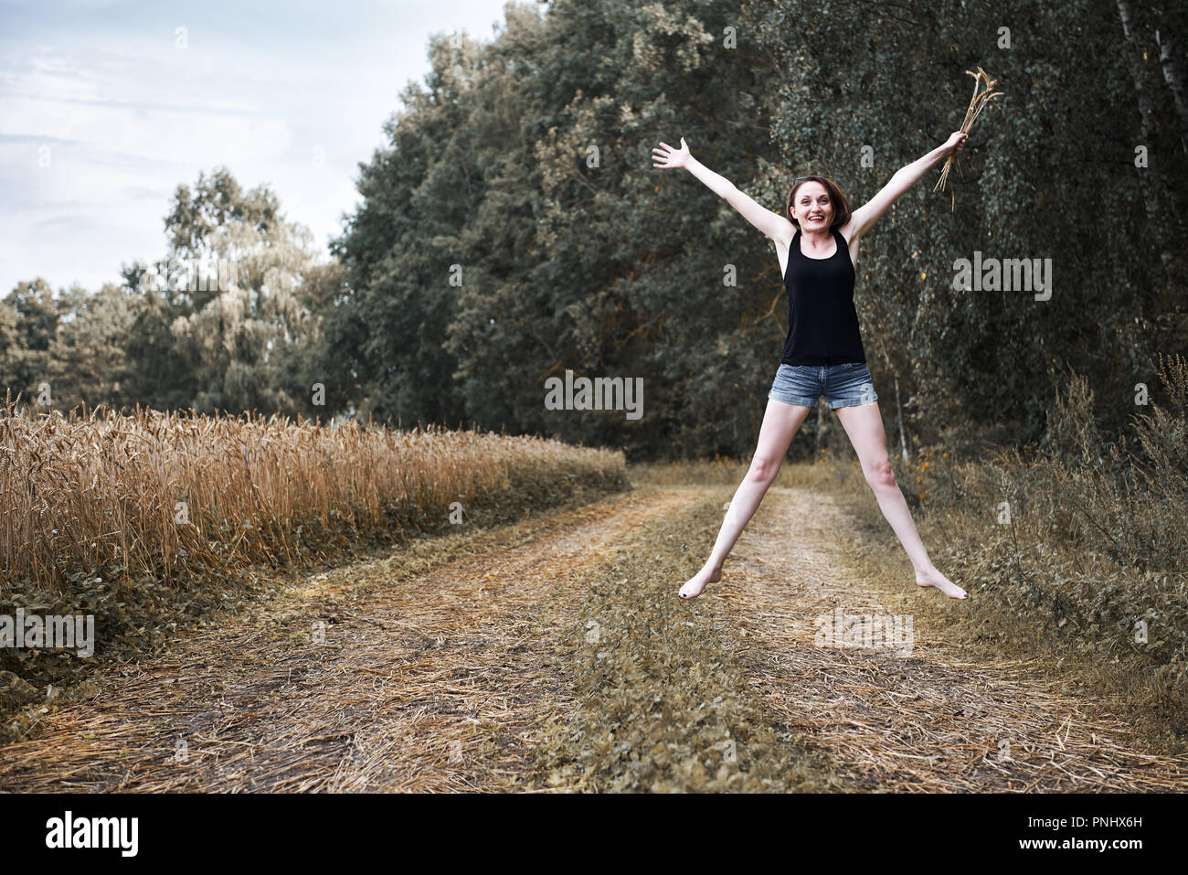 young girl jumping barefoot on the ground road through field and forest ...