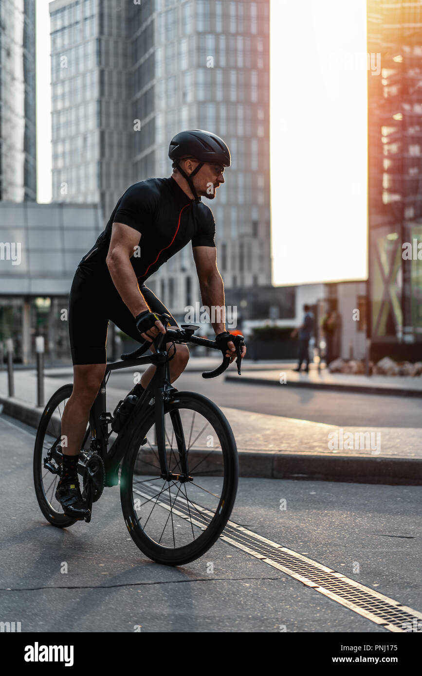 Cyclist riding professional bike next to modern buildings and ...