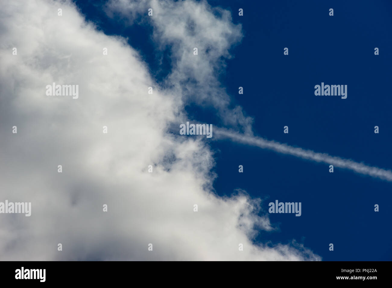 Cumulus summer clouds in the blue sky. White aircraft vapor trail ...