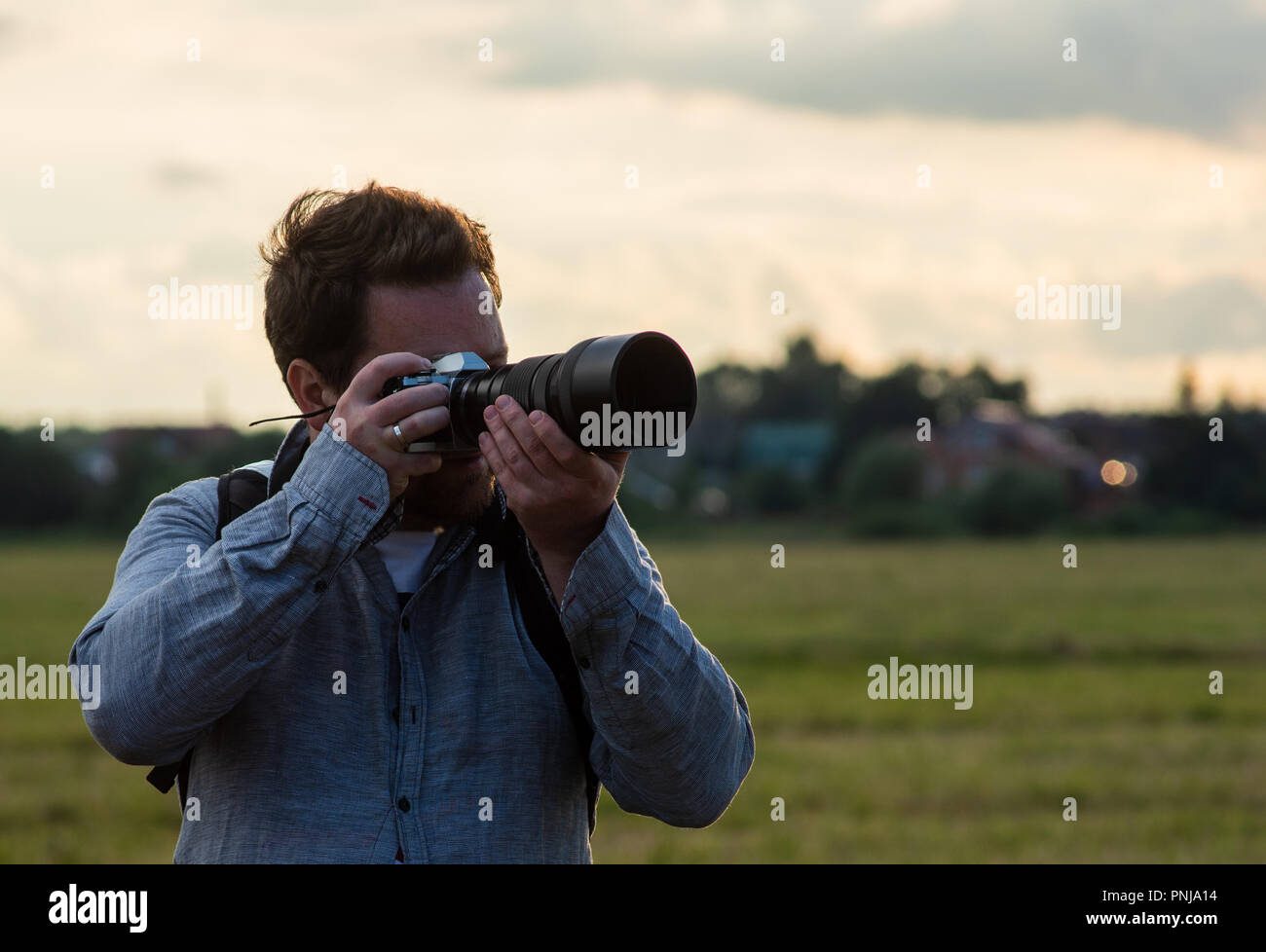 A young white man with a camera walking on the field and taking ...