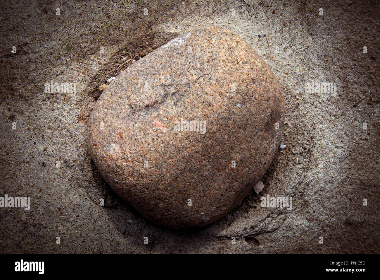 Small round granite stone half fixed in concrete surface, background ...