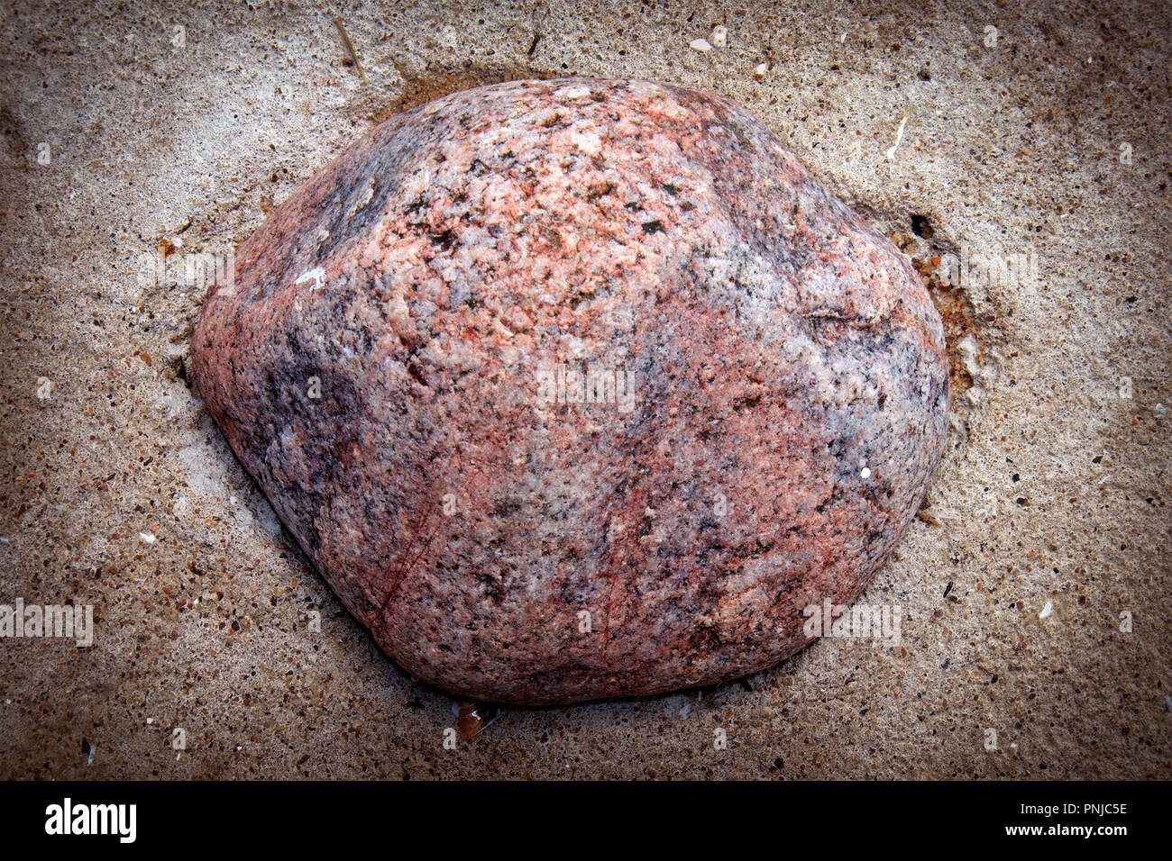 Small round pink granite stone half fixed in concrete surface ...