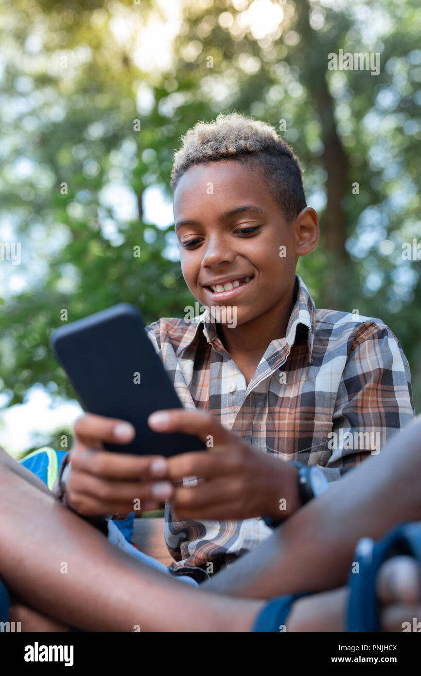 Cute cheerful nice boy looking at his smartphone Stock Photo - Alamy