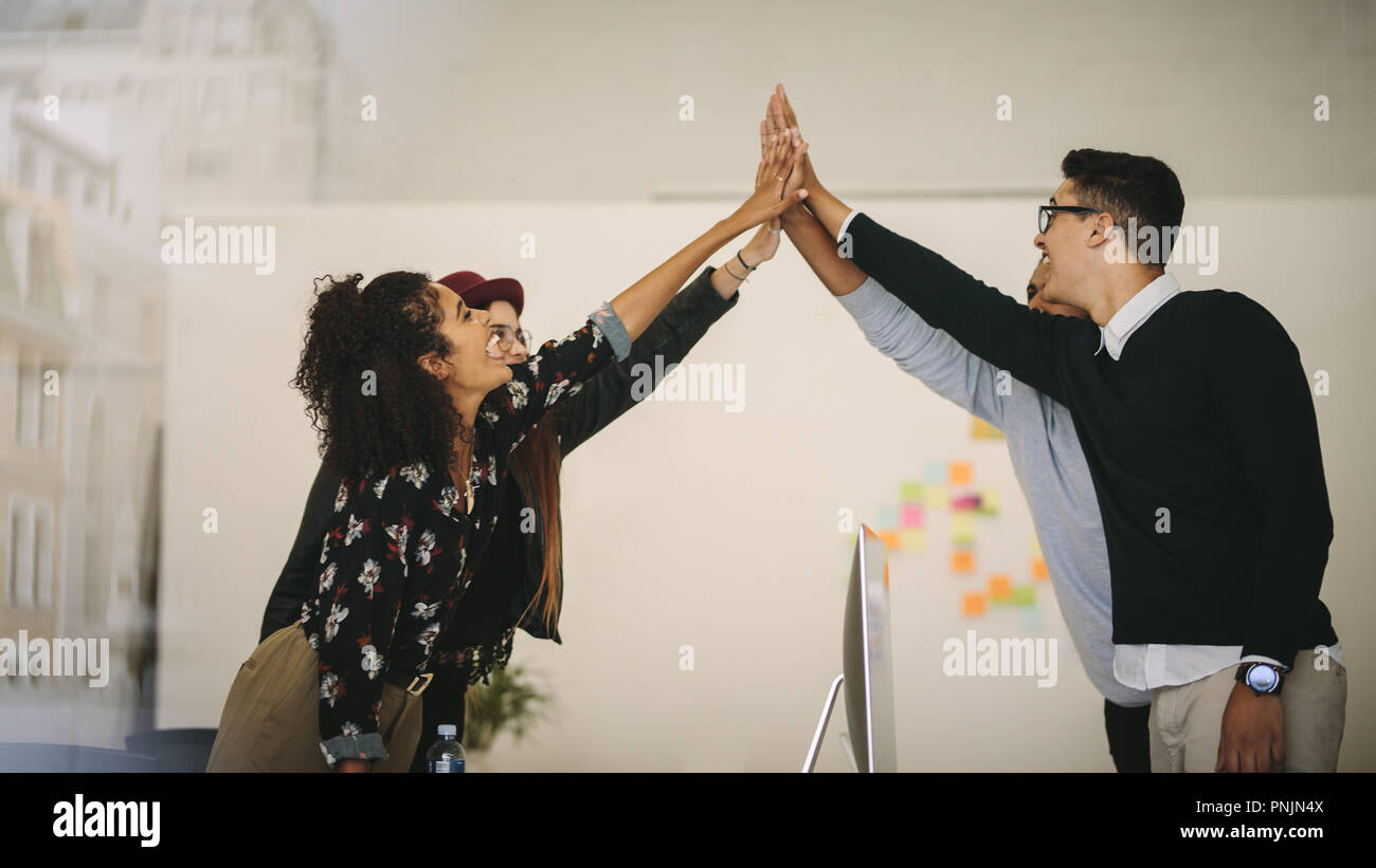 Group of four business partners giving high five to each other standing ...
