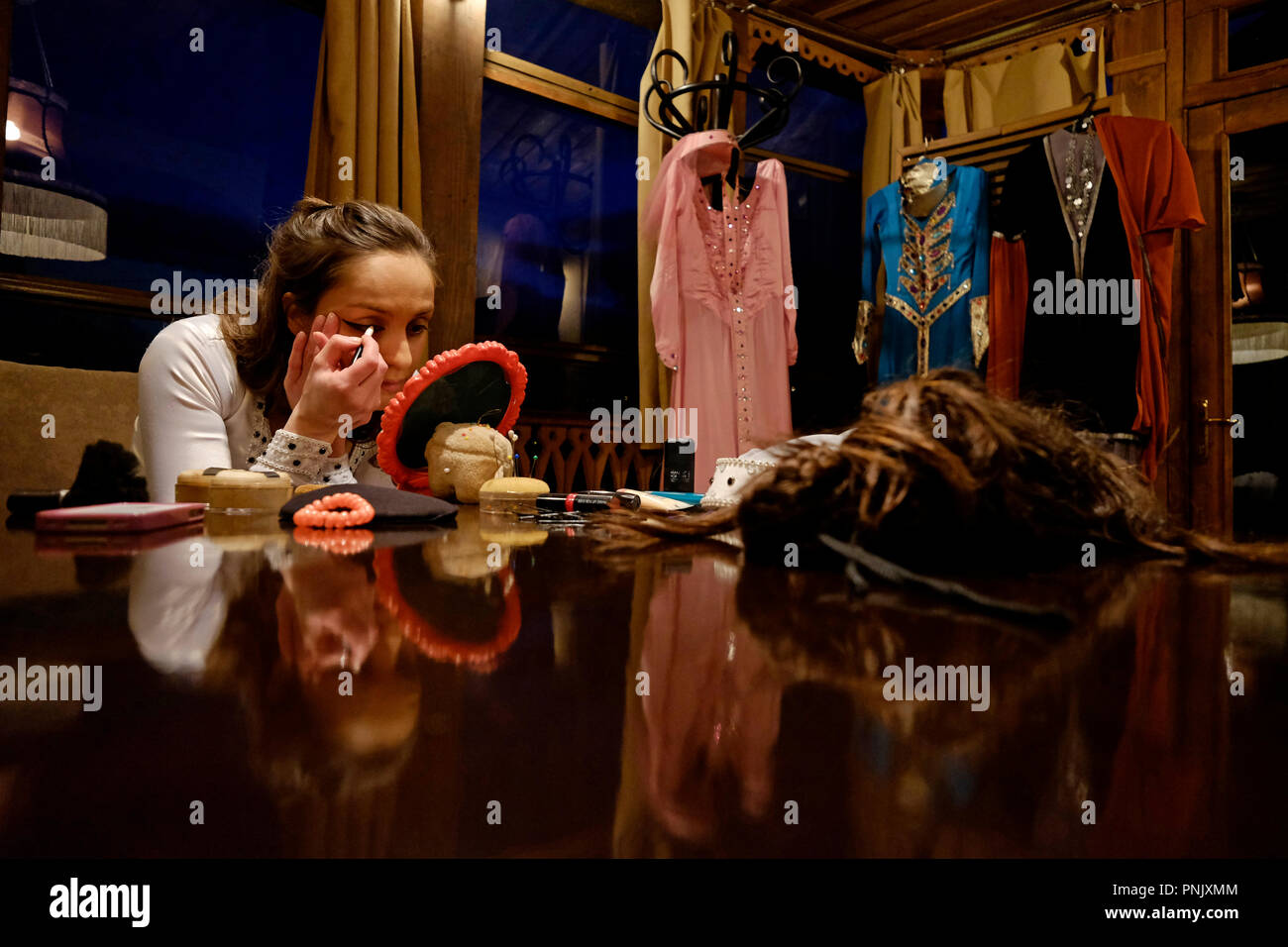 A young dancer looking in the mirror and applying makeup on eyebrow as ...
