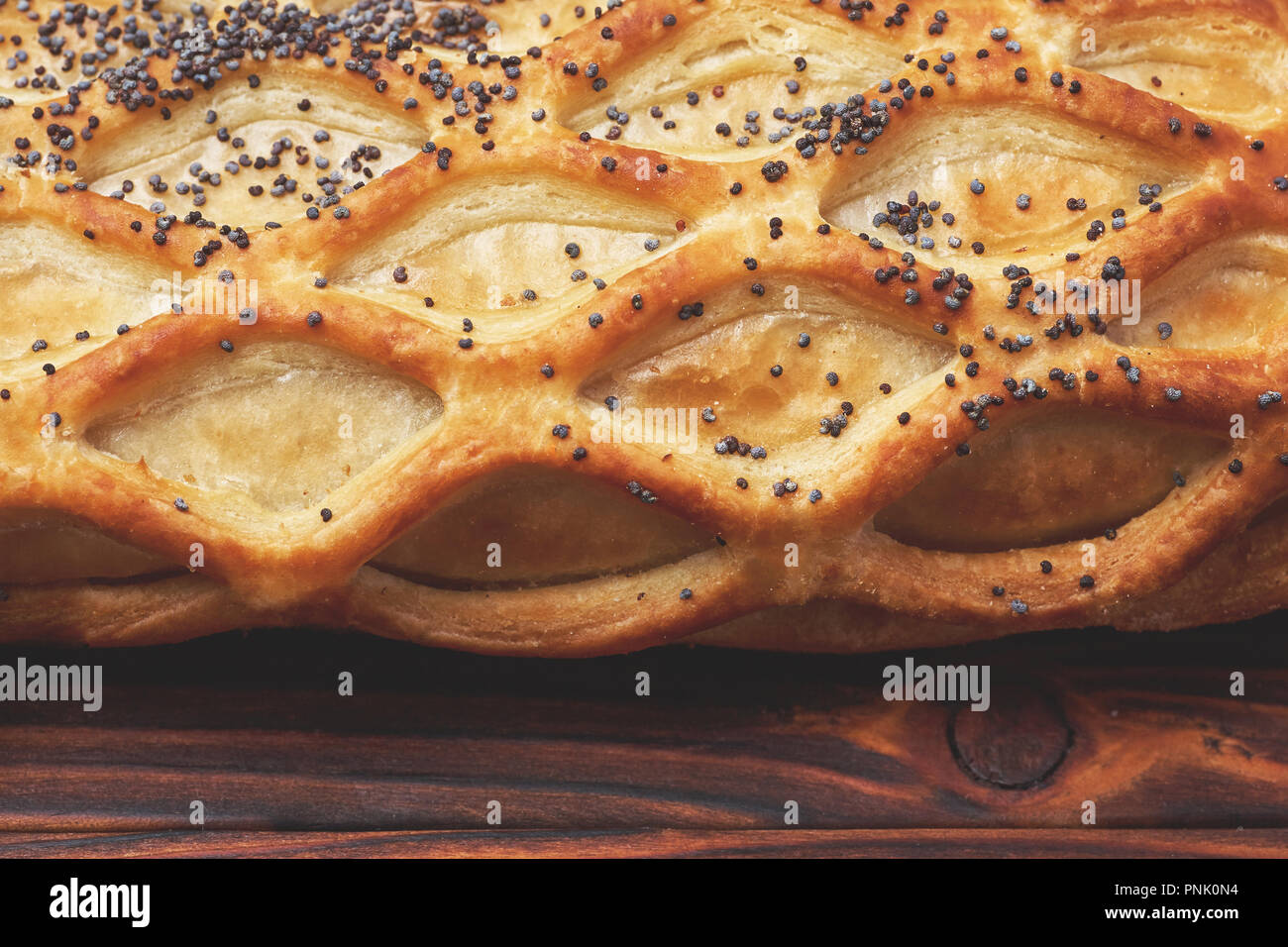 Baked bun with flaky pastry sprinkled with poppy seeds on a dark wooden ...