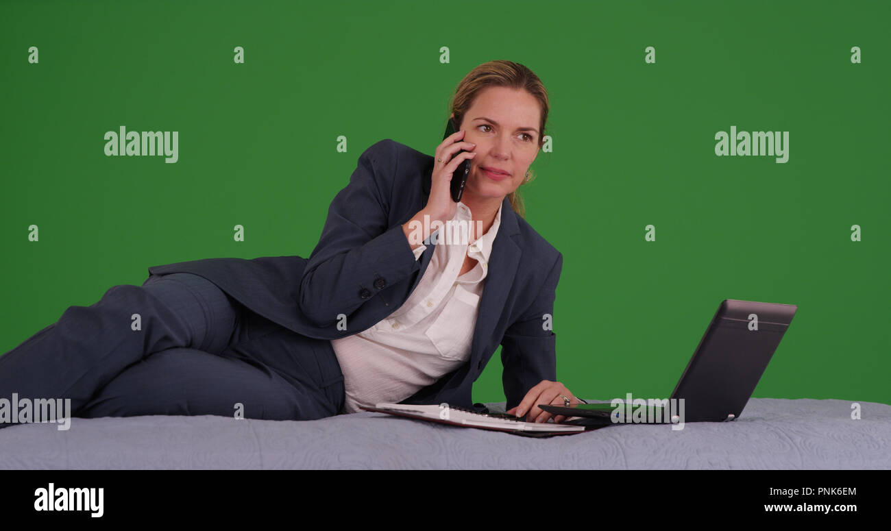 Successful woman in business suit making phone call on bed on green ...