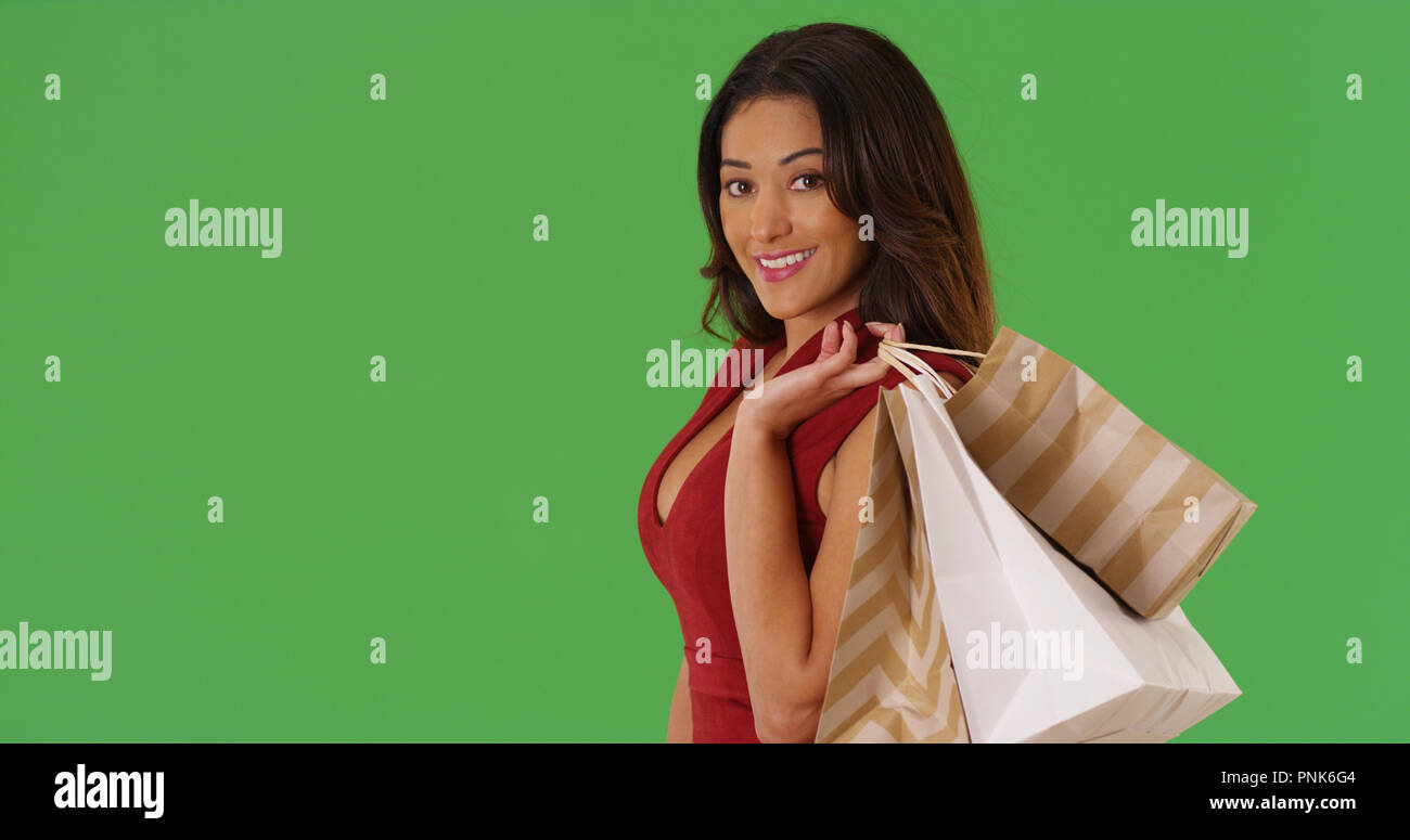 Latina woman holding shopping bags over shoulder smiling on green ...