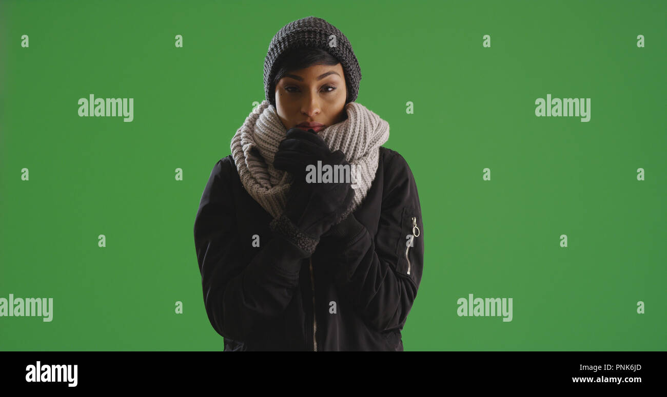 Shivering black female in winter clothes looking at camera on green ...