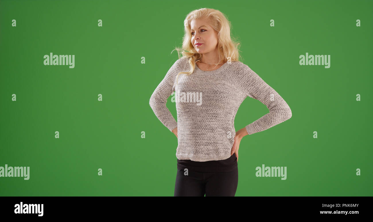 Portrait of white female with hands at hips looking off screen on green ...