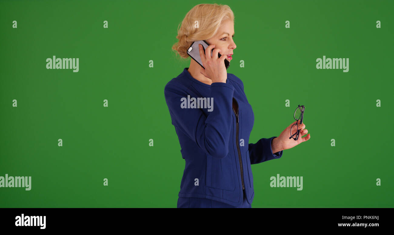 Portrait of female CEO holding glasses talking on cellphone on green ...