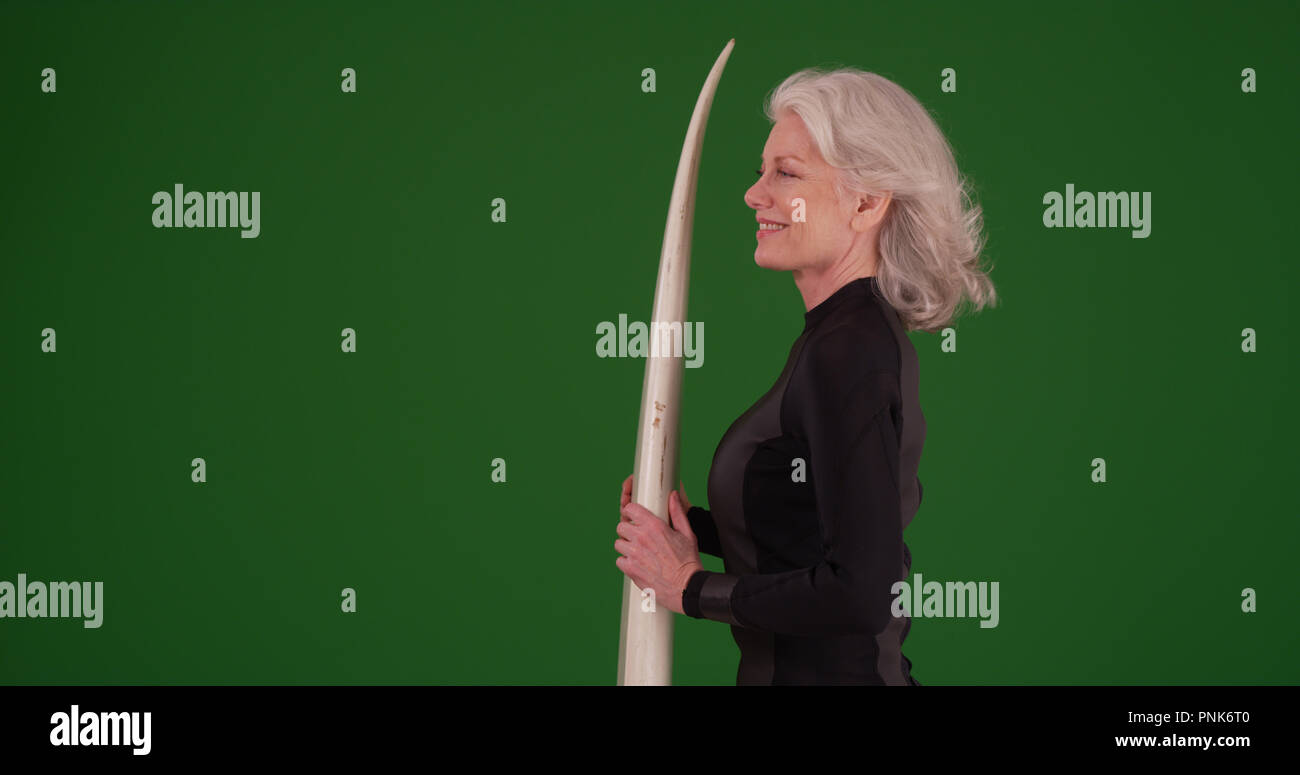 Profile of active white female senior surfer with surfboard on green ...