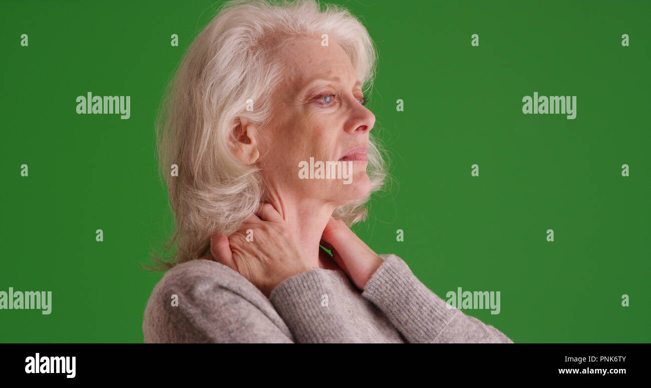 Elderly female with sore neck looking uncomfortable on green screen ...