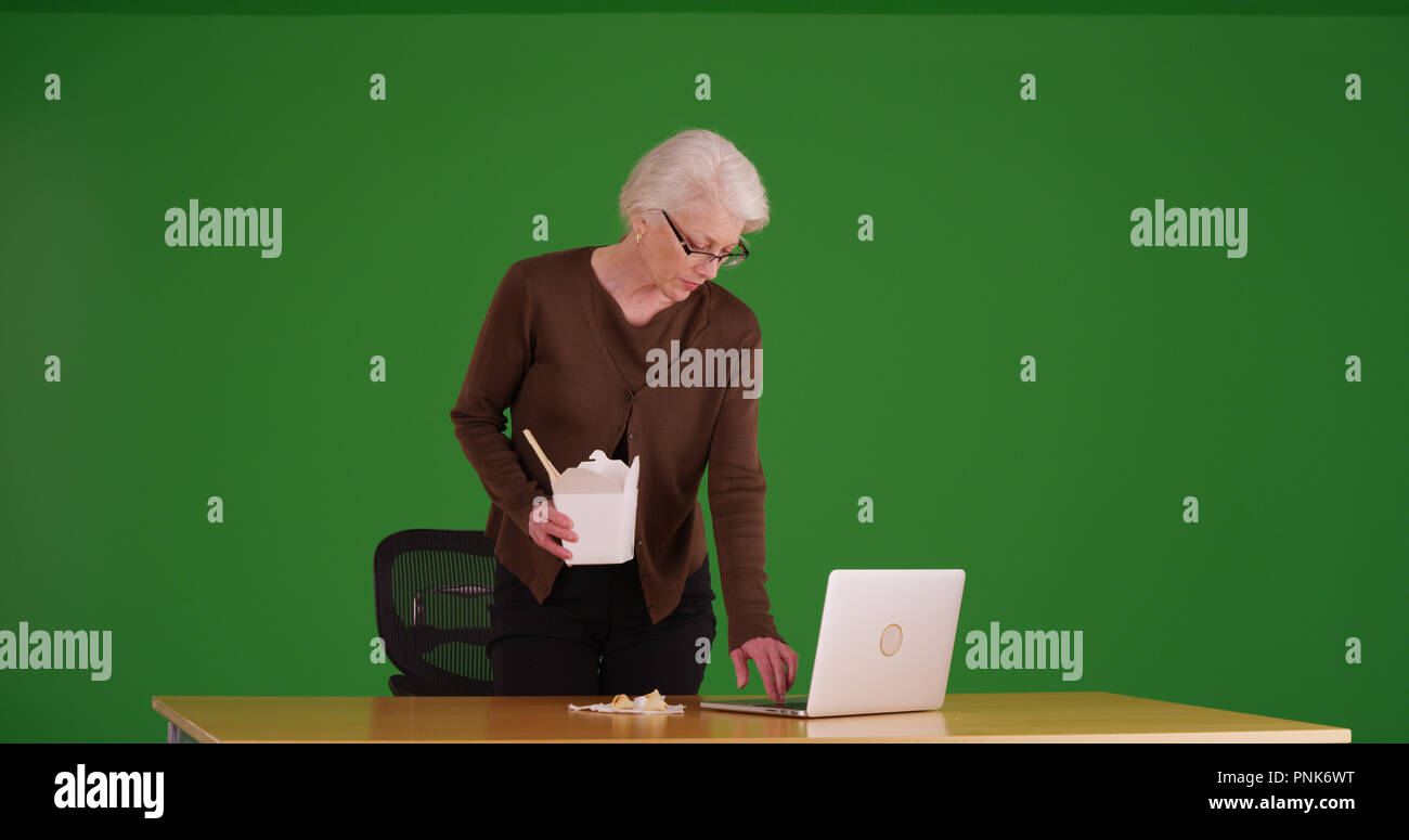 Mature businesswoman using laptop during lunch break on green screen ...