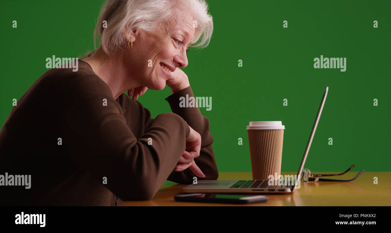 side-profile-of-happy-old-woman-scrolling-on-laptop-with-coffee-on-green-screen-stock-photo-alamy
