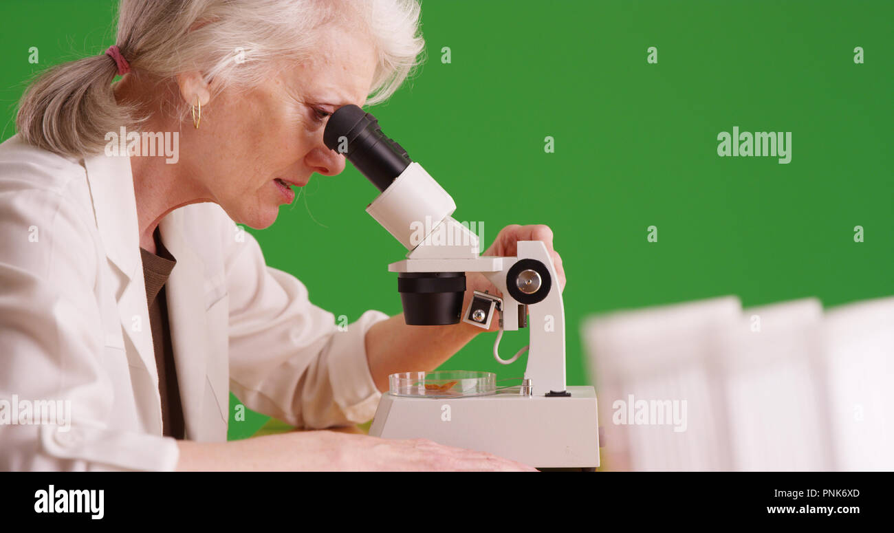 Senior scientist examining test sample with microscope in lab on green ...
