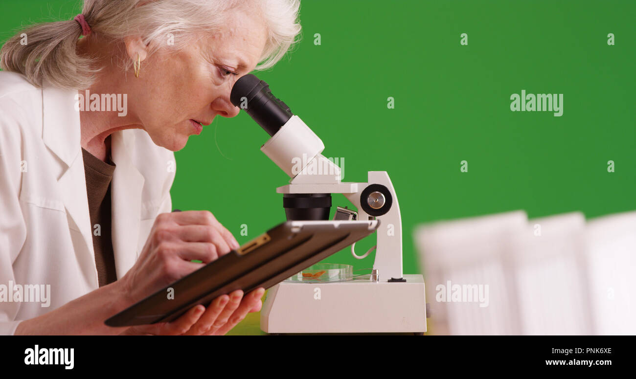 Female researcher using microscope recording data on tablet on green ...