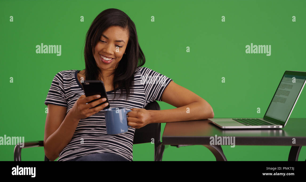 Smiling black woman with coffee using mobile device at cafe on green ...