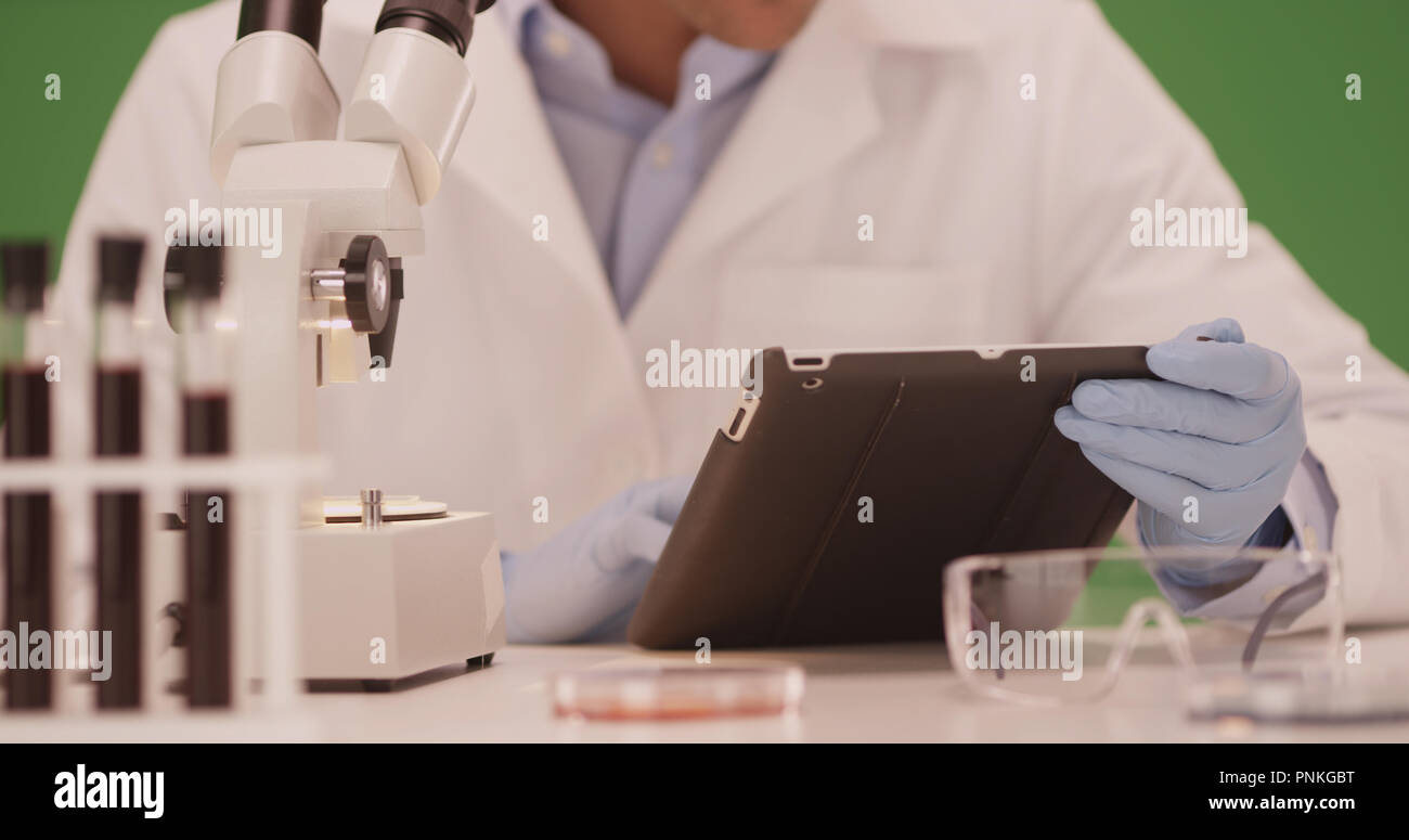 Millennial Latino medical scientist using tablet computer on green ...