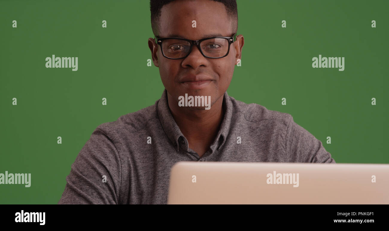 Millennial man sitting at desk with computer smiling on green screen ...