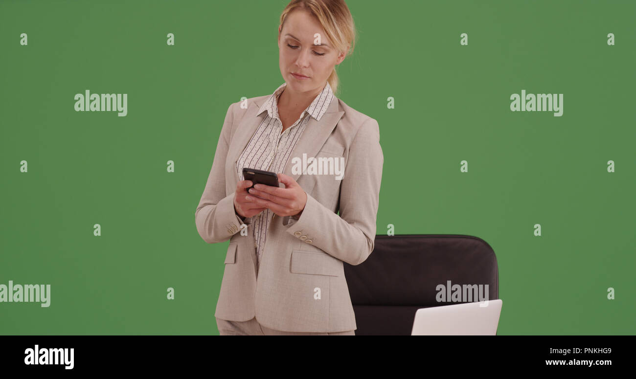 Businesswoman texting on smartphone at desk on green screen Stock Photo ...