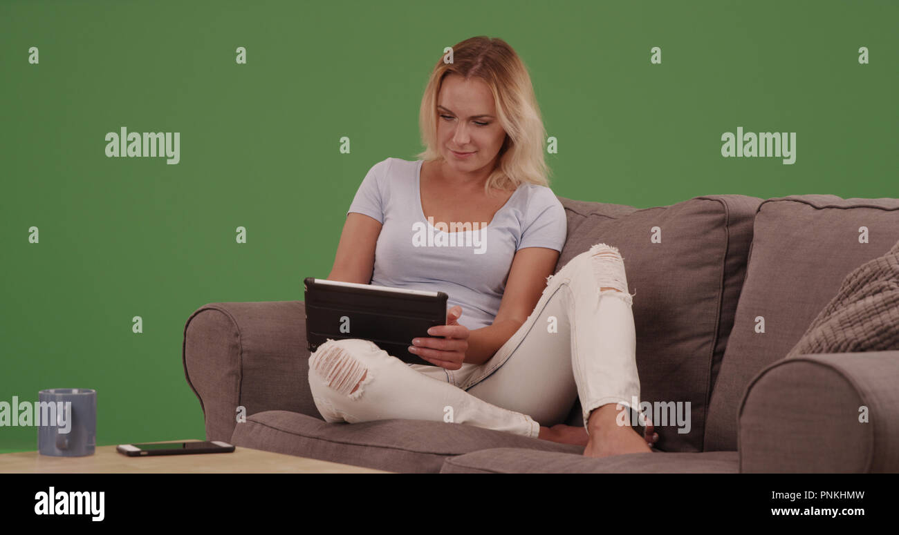 Blonde white woman using tablet on couch on green screen Stock Photo ...