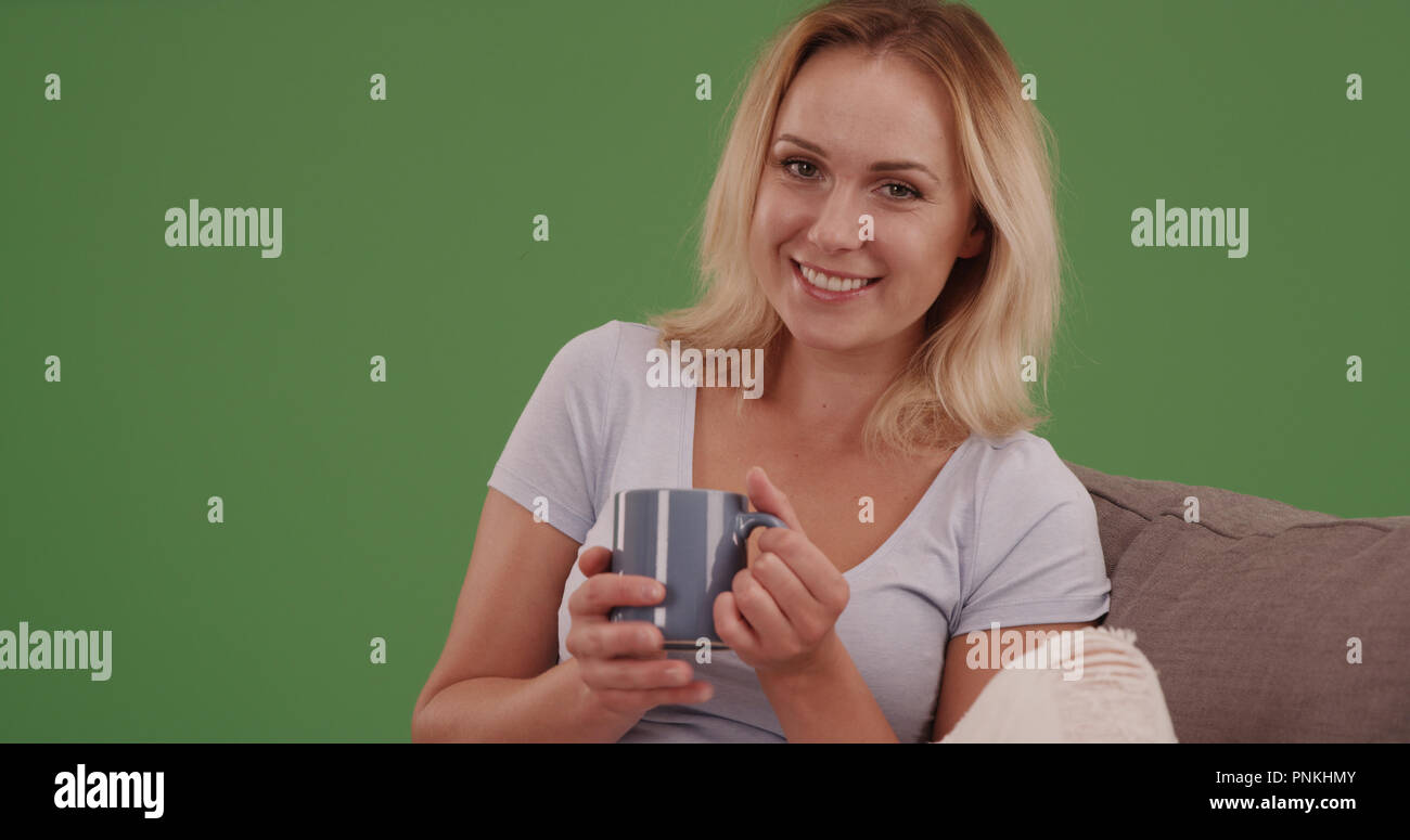 Woman sitting on couch holding coffee mug looking at camera on green ...