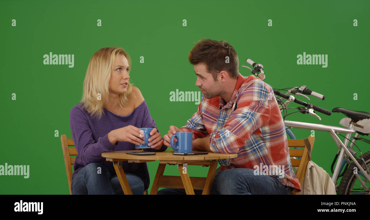 Millennial white couple sitting at cafe table drinking coffee on green ...