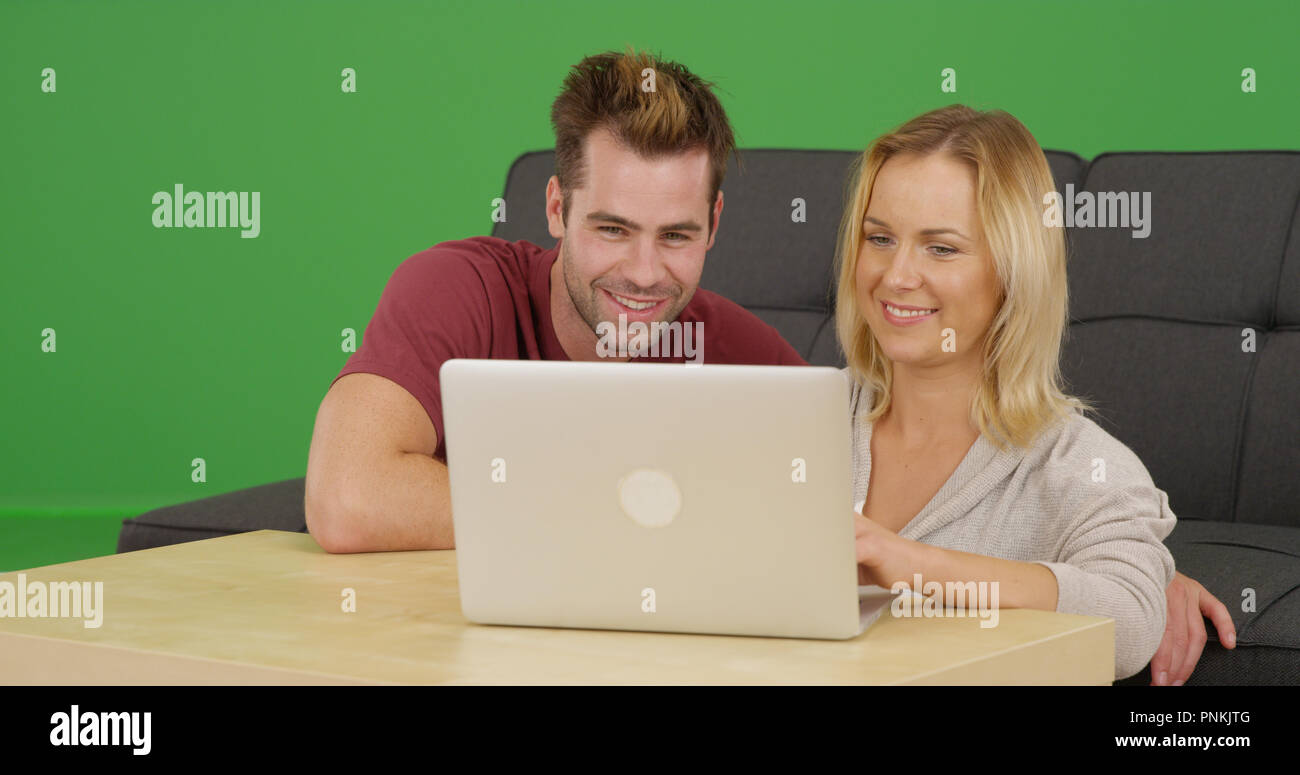 Millennial couple using laptop computer together at home on green ...