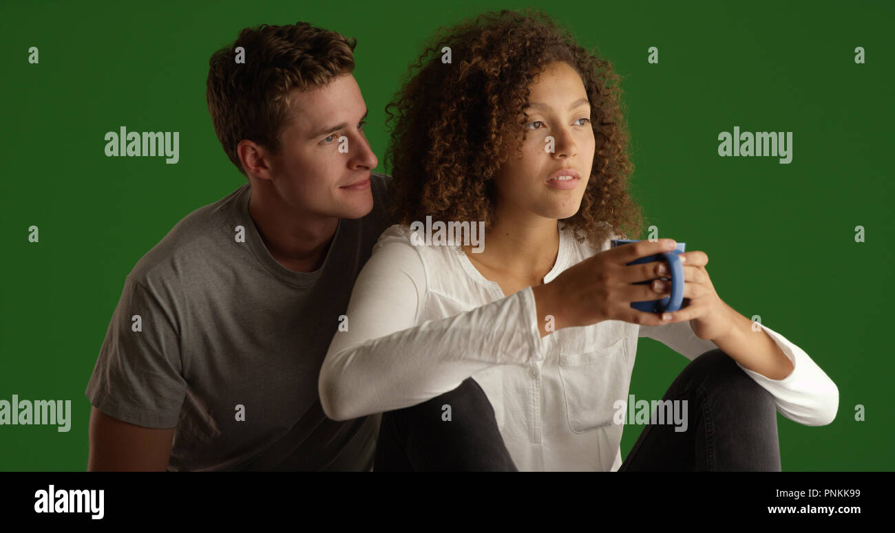 Young interracial couple sitting together looking offscreen on green ...