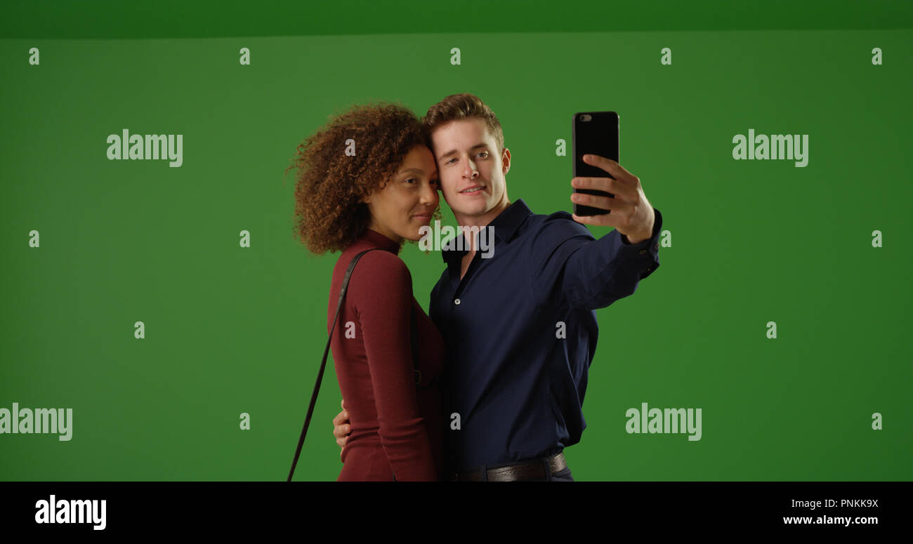 Happy interracial couple using smartphone to take selfie on green ...