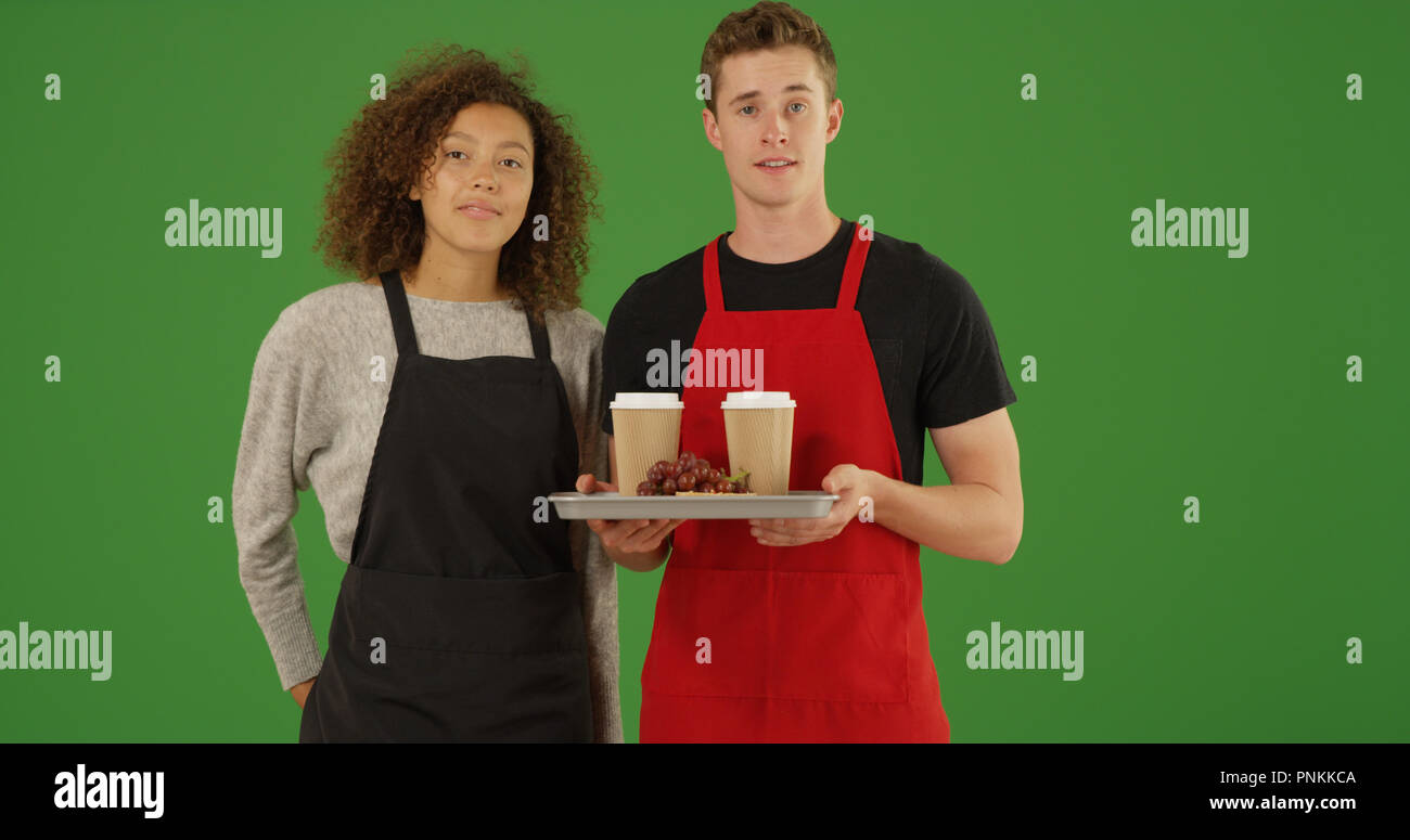 Two waiters with tray of food and drinks looking at camera on green ...