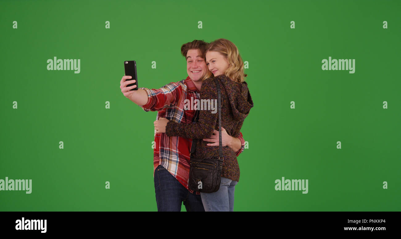 Young millennial couple posing for smartphone selfie together on green ...