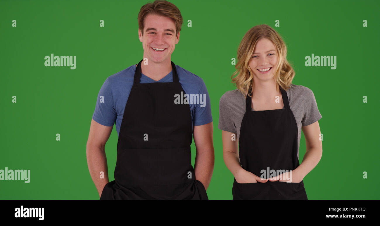 Smiling male and female restaurant employees posing in aprons on green ...