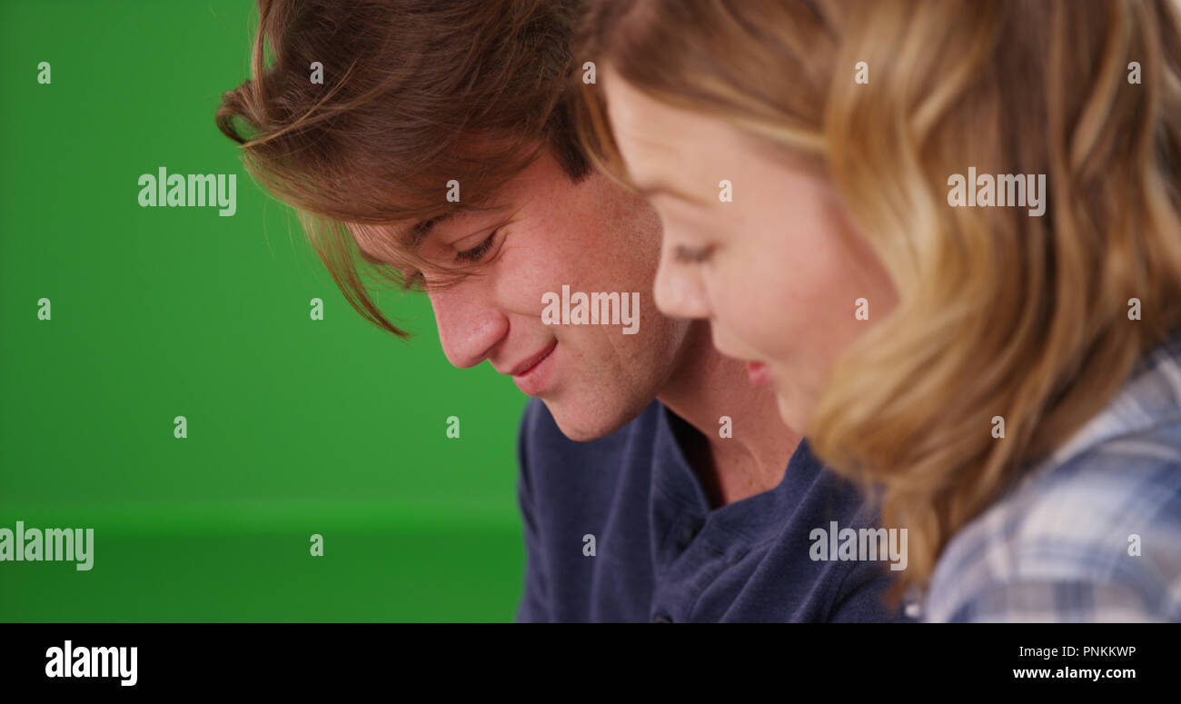 Caucasian male and female looking down at tablet or laptop on green ...