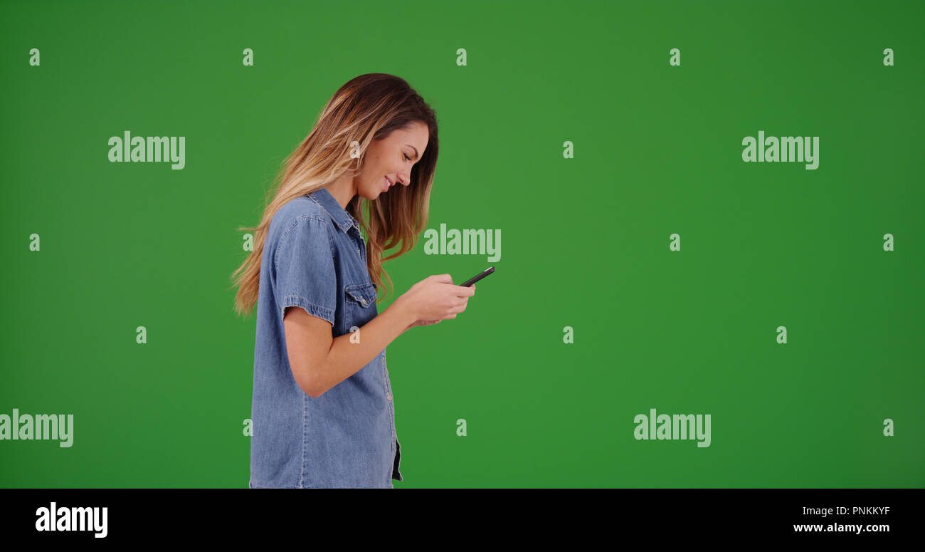 Side profile of attractive millennial girl texting on phone on green ...