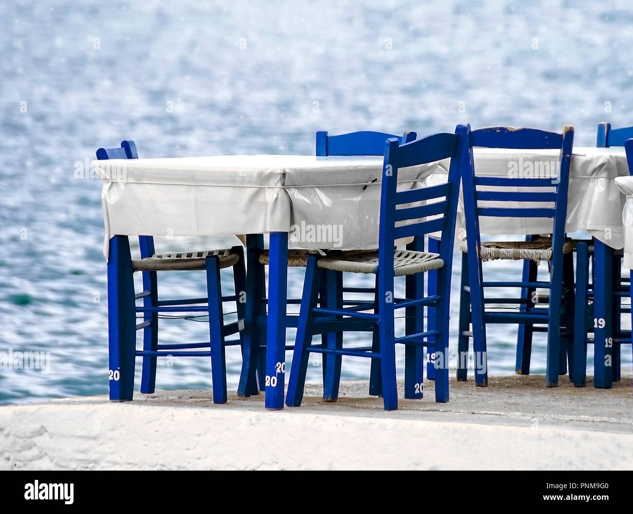 Tables and blue chairs by the seaside. Greece Stock Photo - Alamy