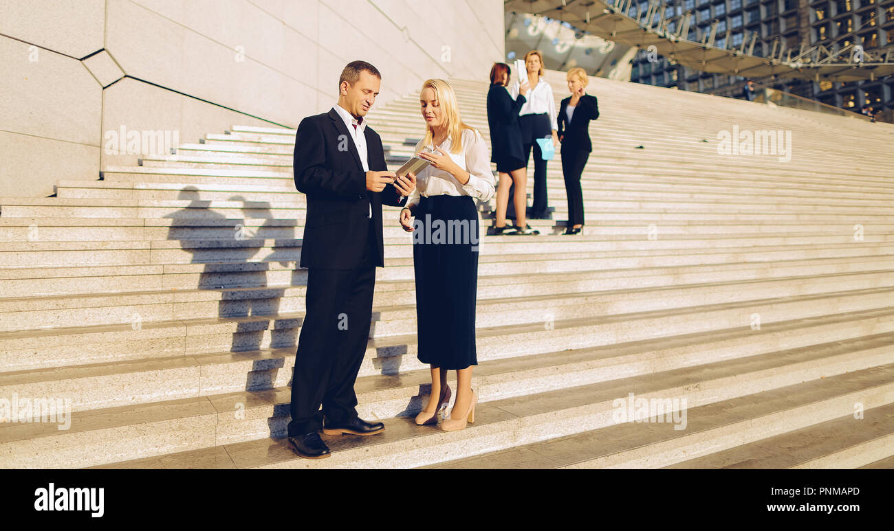 Boss keeping tablet and speaking with blonde secretary on stairs with ...