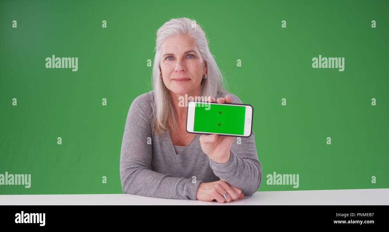 Serious mature white lady showing cellphone to camera on greenscreen ...