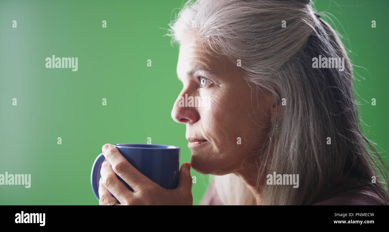 Closeup side profile of old white lady with coffee cup on greenscreen ...