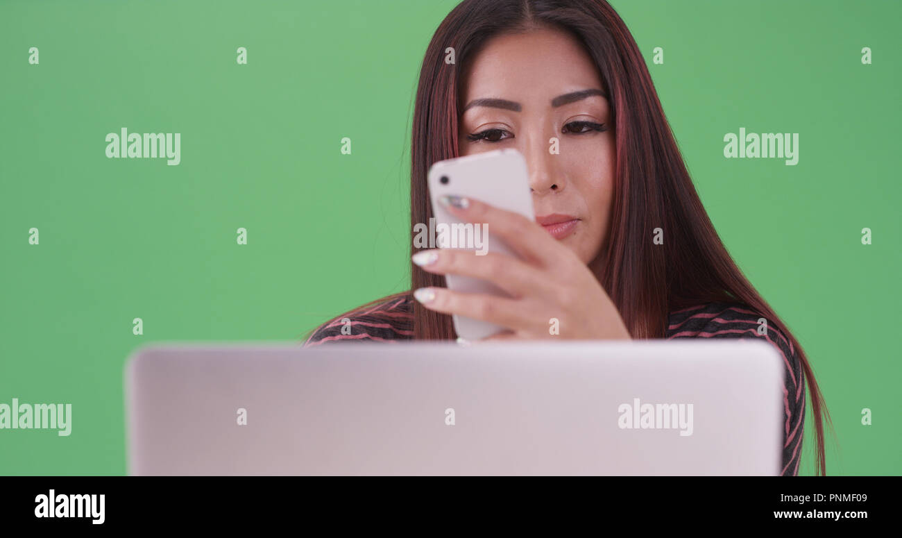 Asian woman using smartphone and laptop on green screen Stock Photo - Alamy