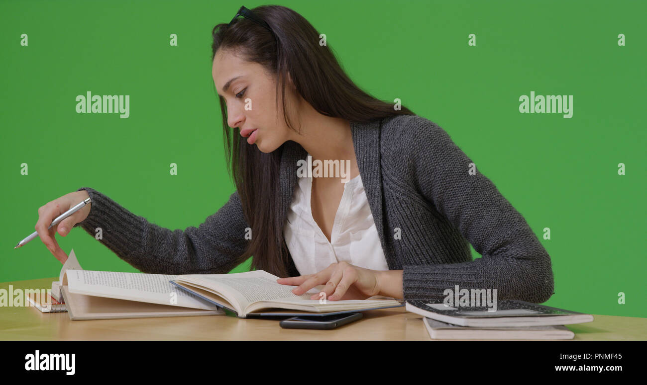 A college student does her homework sitting at desk on green screen ...