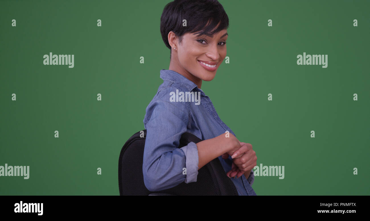 Smiling black woman looking back at camera over chair on green screen ...