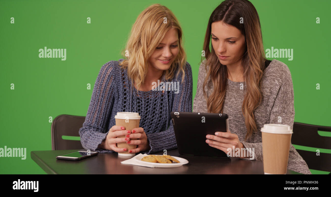 Lovely couple of girls sitting and sharing tablet computer on green ...