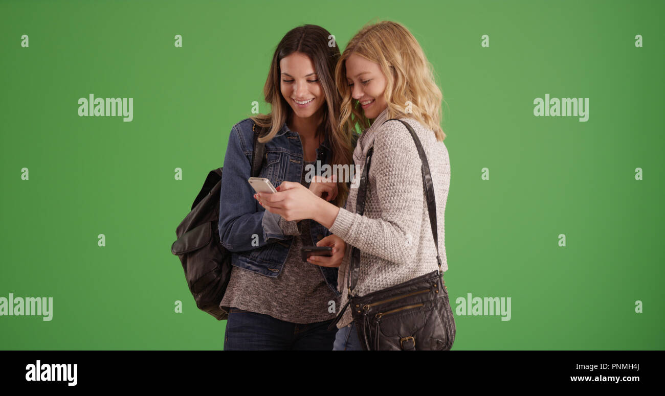 Pair of lovely Caucasian ladies sharing phone standing on green screen ...