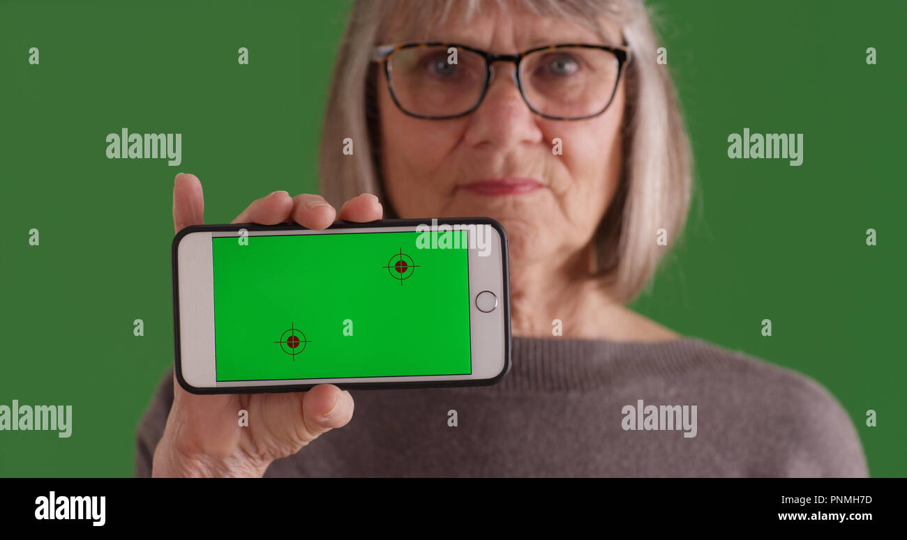 Closeup of old lady showing green screen phone display to camera on ...