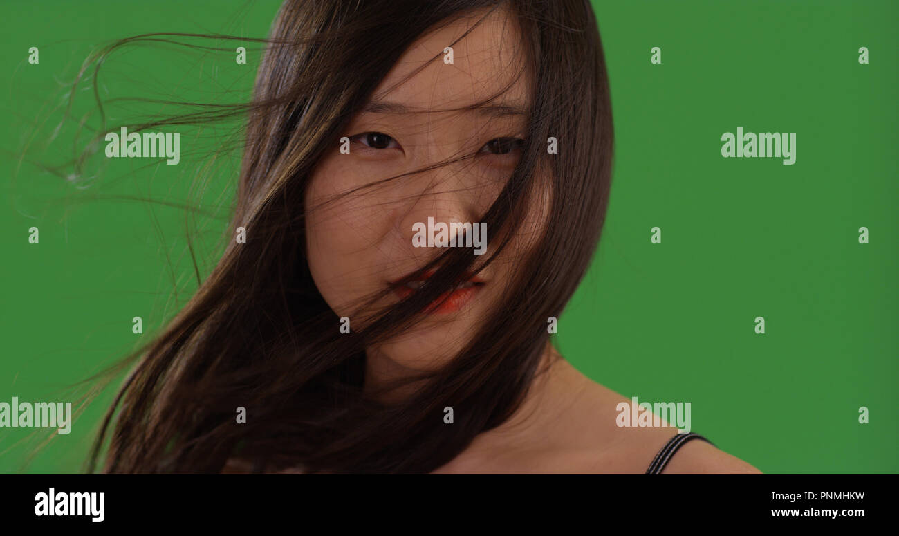 Asian woman looking at camera with hair blowing in wind on green screen ...