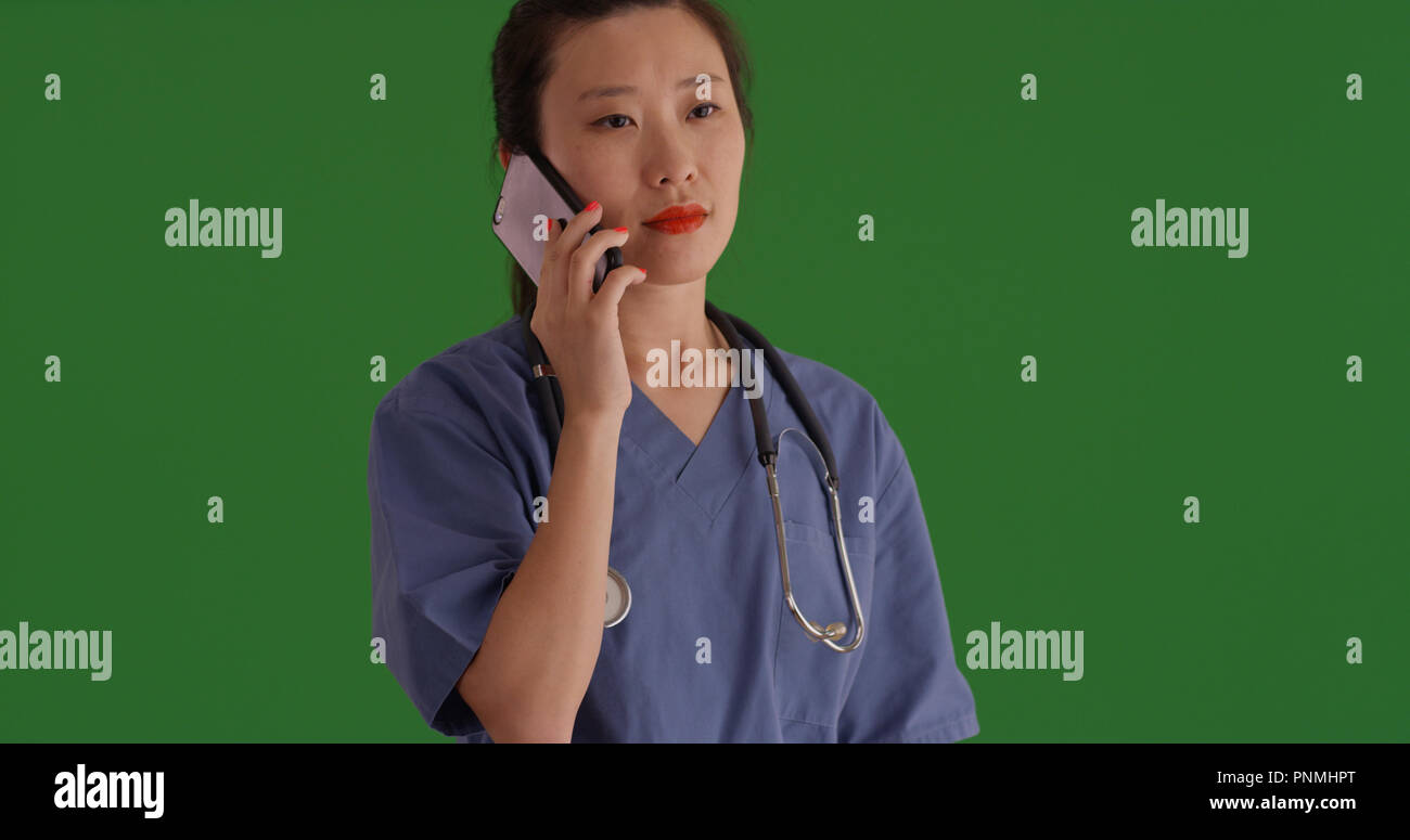 Young Asian nurse using smartphone to make phone call on green screen ...